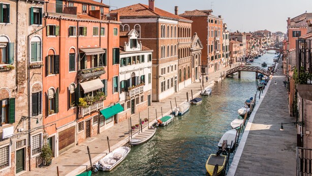 Um canal ladeado por edifícios históricos, passagens estreitas e barcos atracados na água.