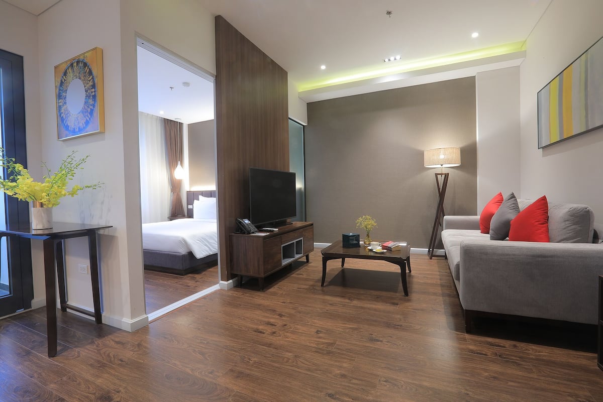 Quarto de hotel moderno com cama, televisão, sofá e mesa de centro.