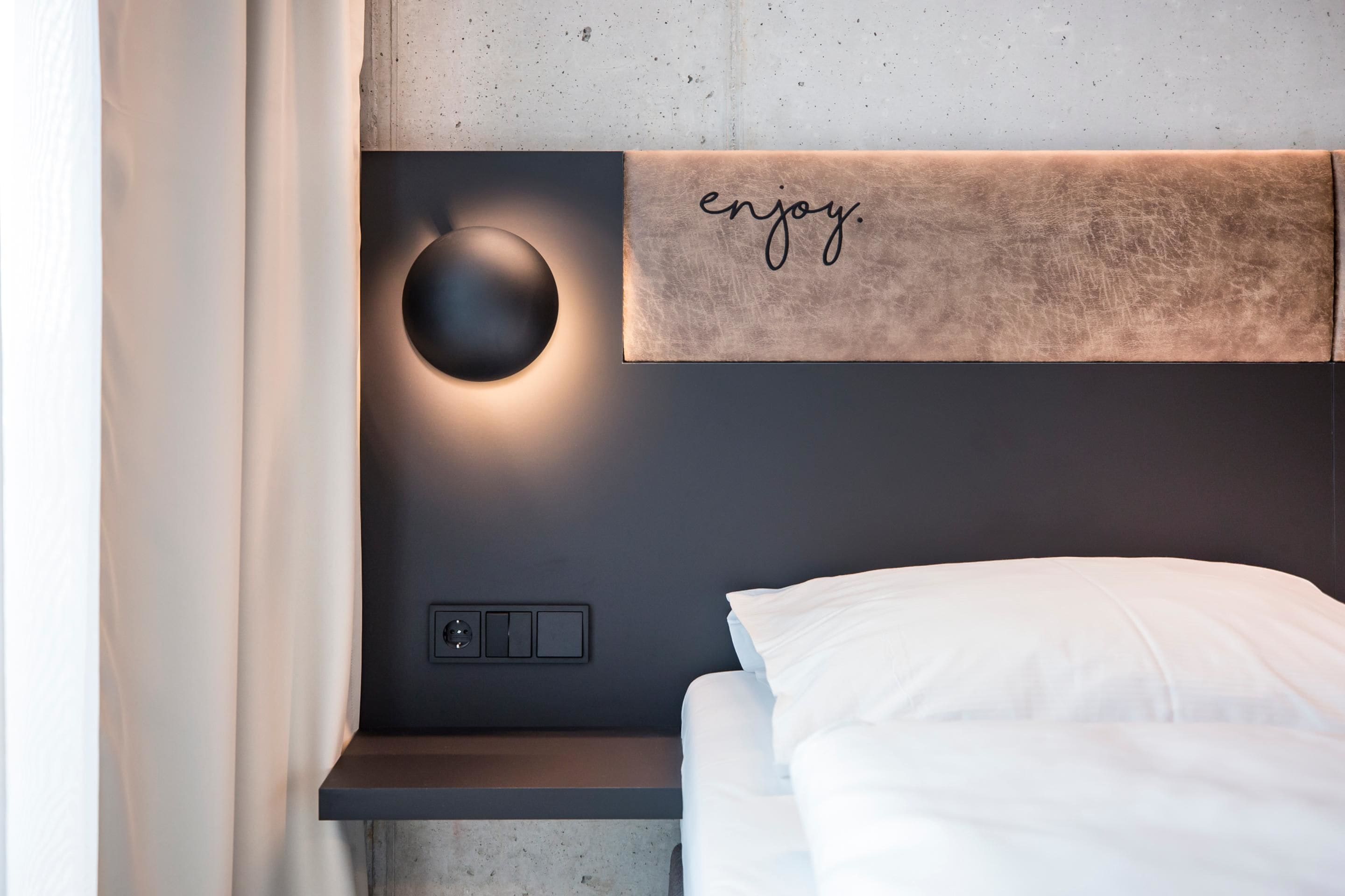 Quarto moderno com cama, mesa de cabeceira, prateleira na parede com uma placa e luminária de parede.