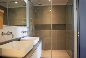 Uma casa de banho moderna com duas lavatórios, chuveiro com divisória de vidro e um espelho grande.