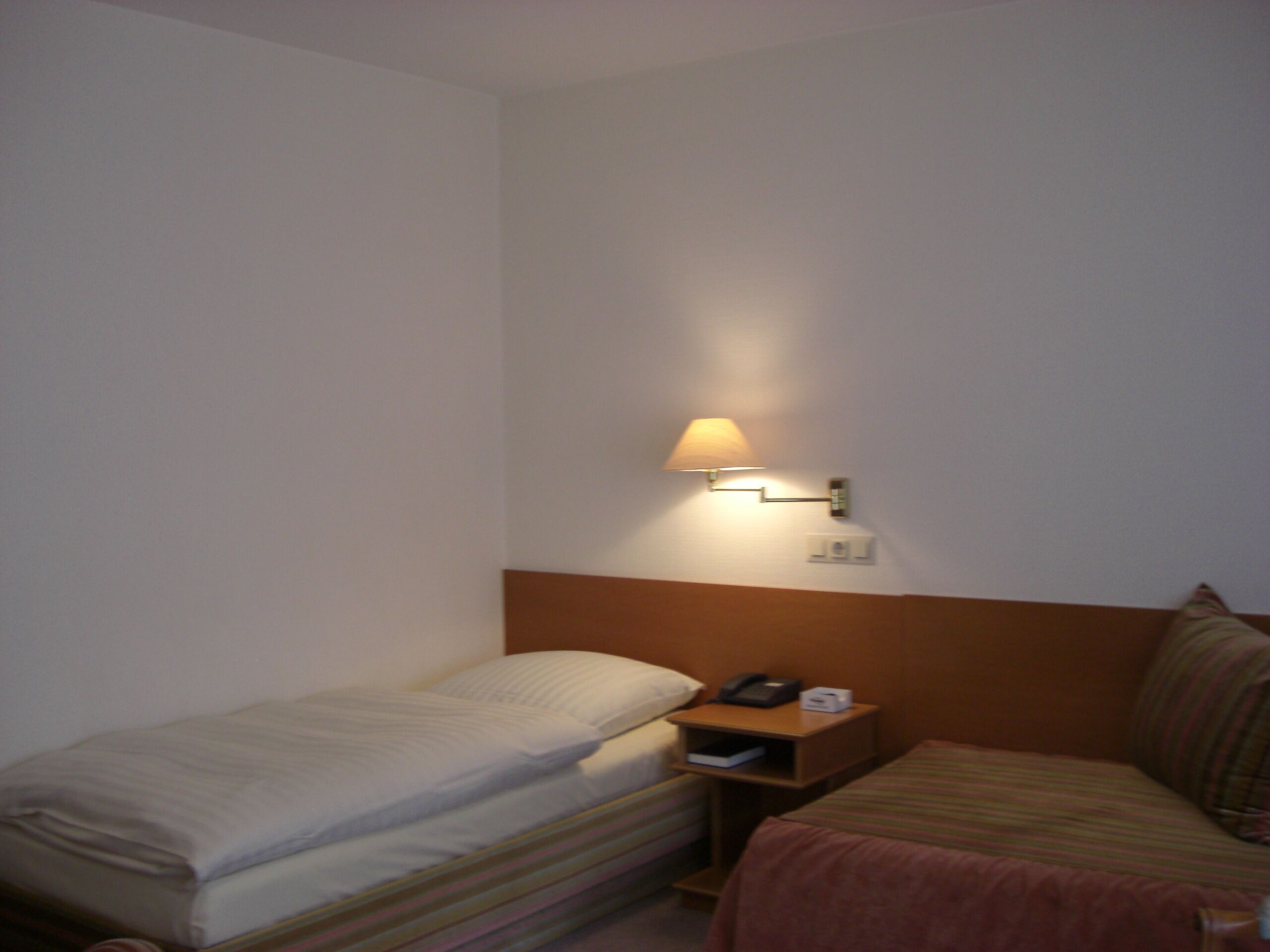 Um quarto de hotel pequeno com duas camas, uma mesa de cabeceira com abajur e um telefone.