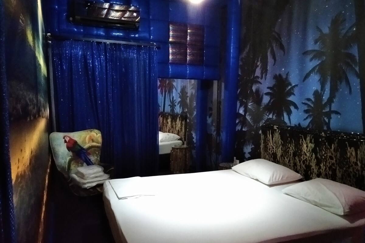 Quarto com cama, uma cadeira e um mural de palmeiras.