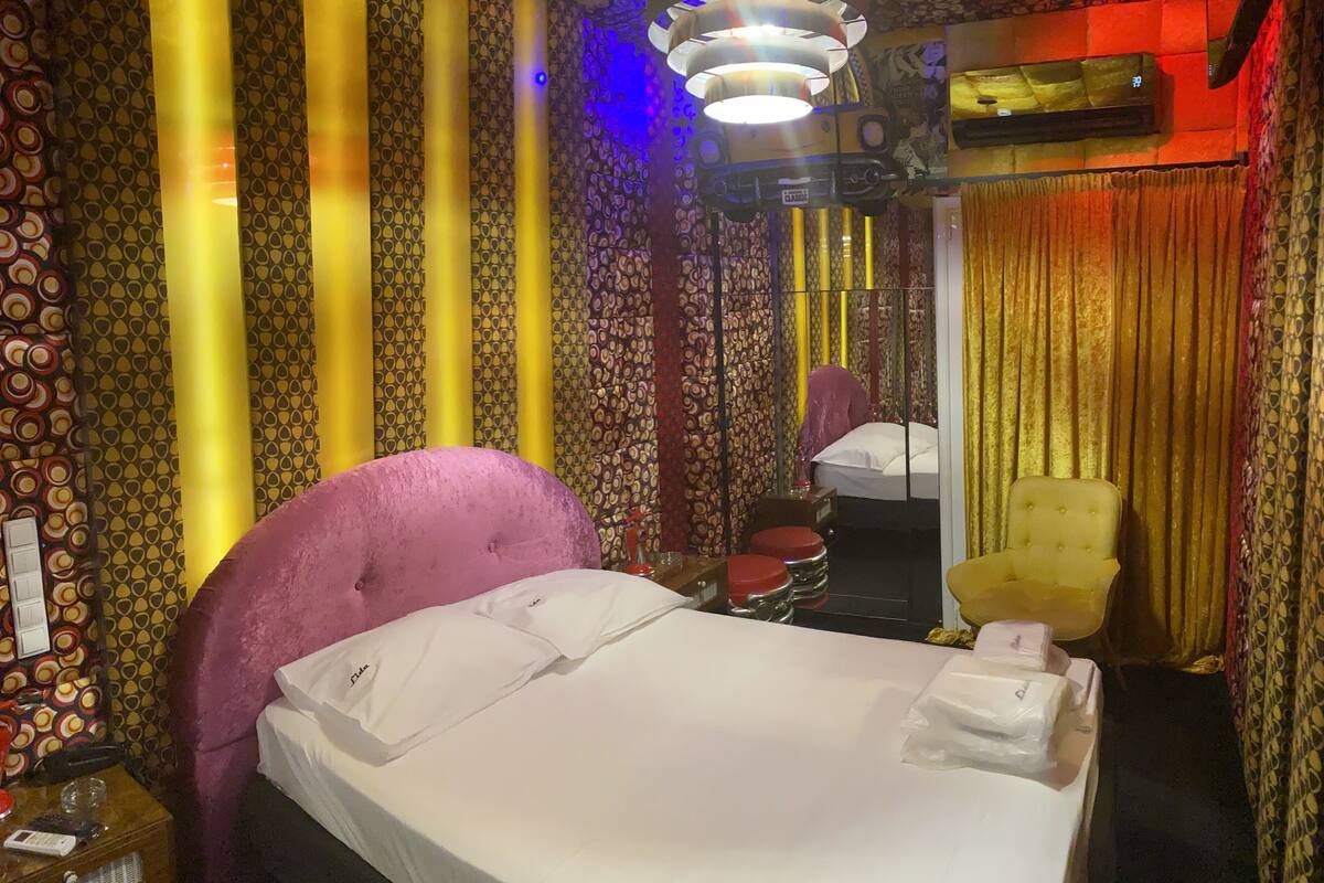 Quarto de hotel com uma cama grande, uma mesinha de vaidade com espelho, uma cadeira e uma pequena mesa com telefone e um copo.