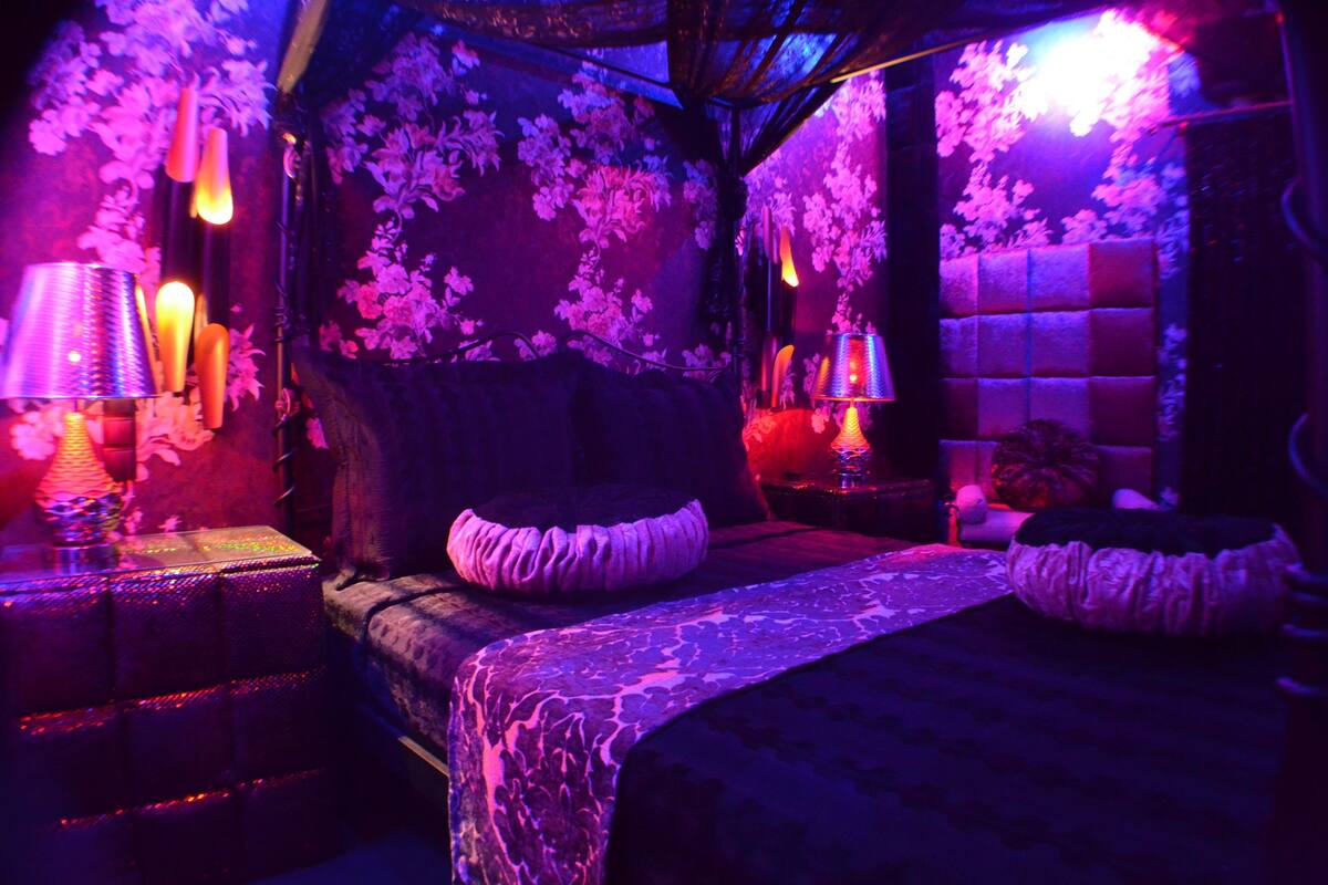 Um quarto com pouca luz, uma cama, papel de parede floral e duas mesas de cabeceira com abajures.