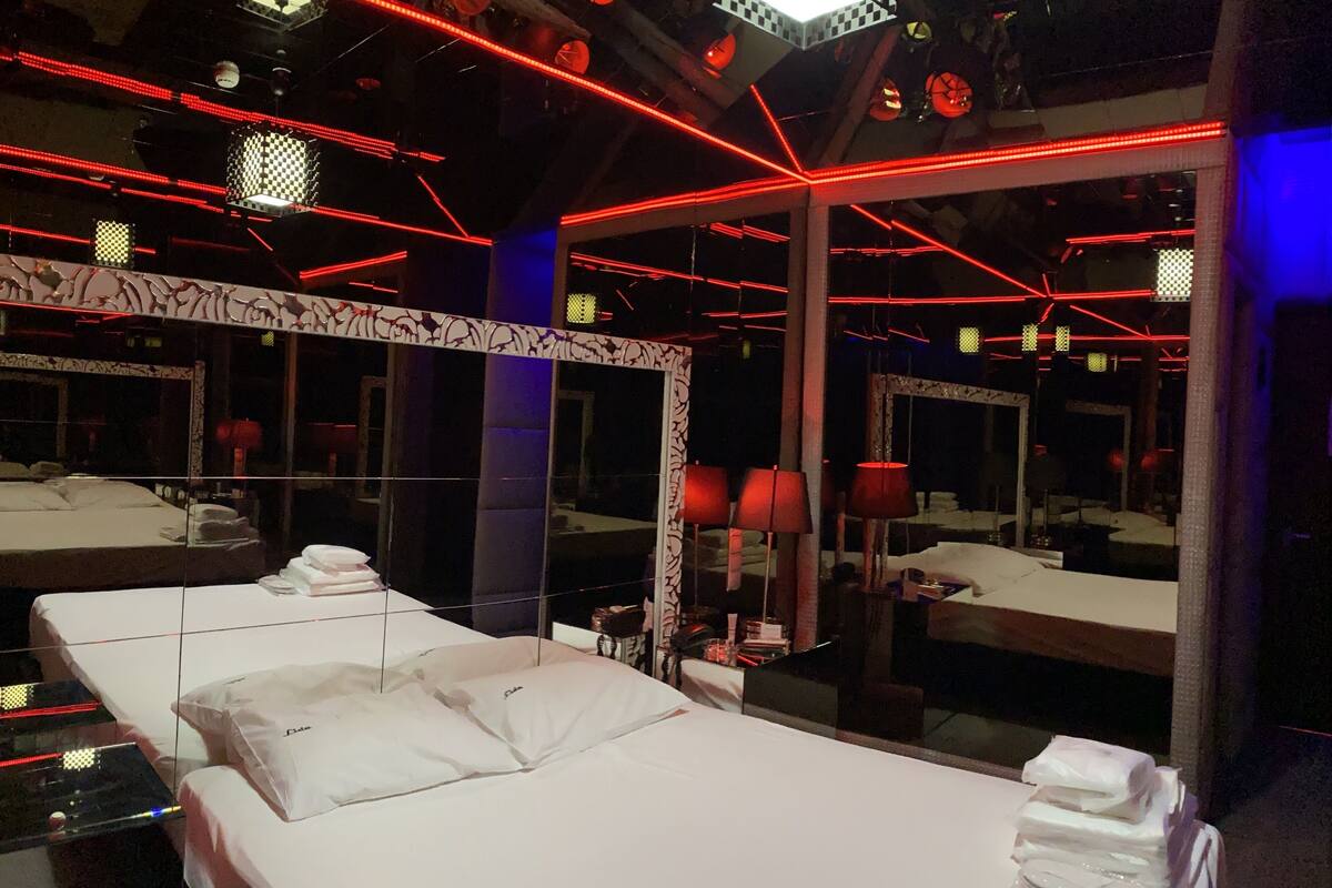 Quarto de hotel com duas camas, um espelho grande e detalhes de iluminação em vermelho.
