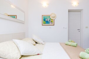 Cama bem arrumada com travesseiros, um quadro na parede, um chapéu e uma toalha ao lado.