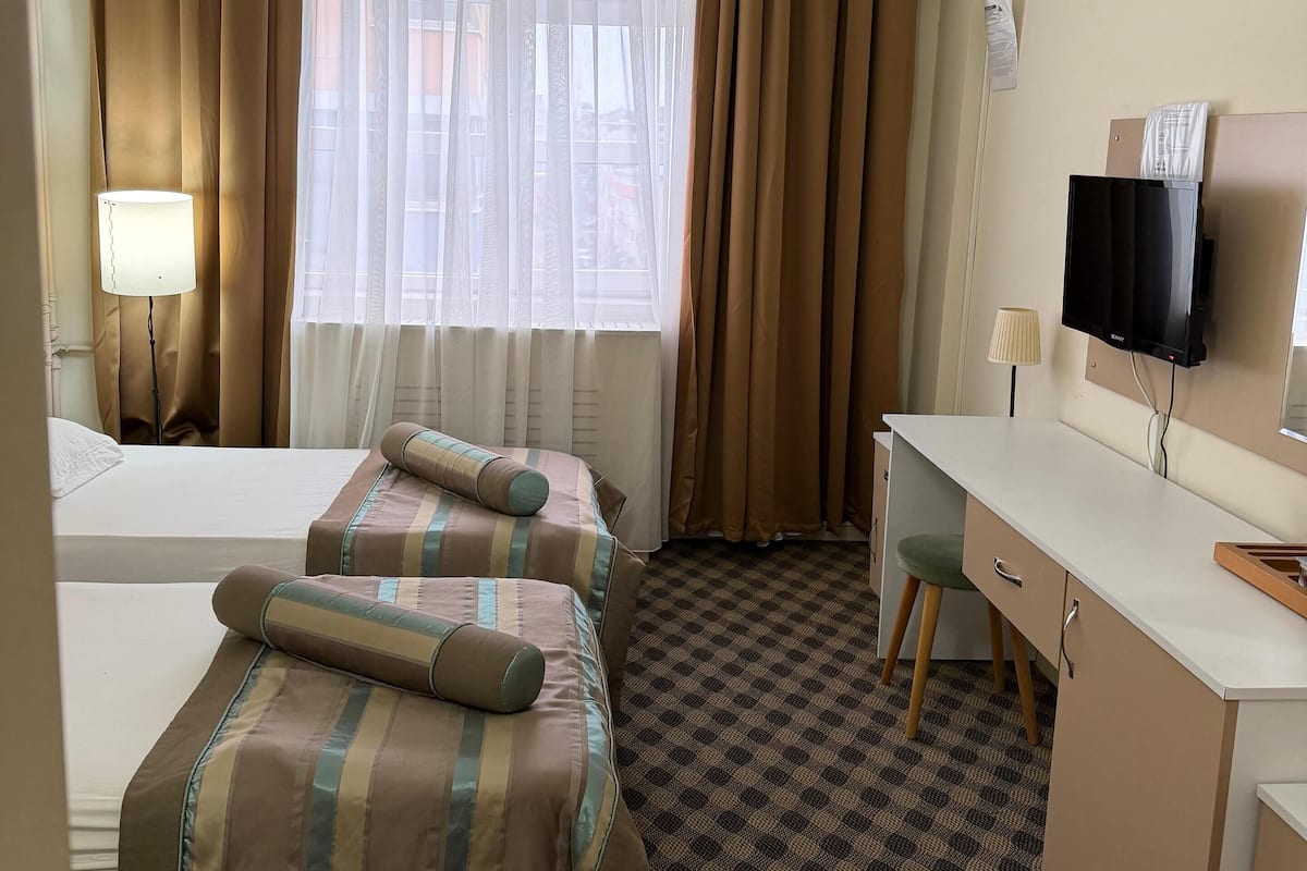 Quarto de hotel com duas camas, uma escrivaninha, televisão e ar condicionado.
