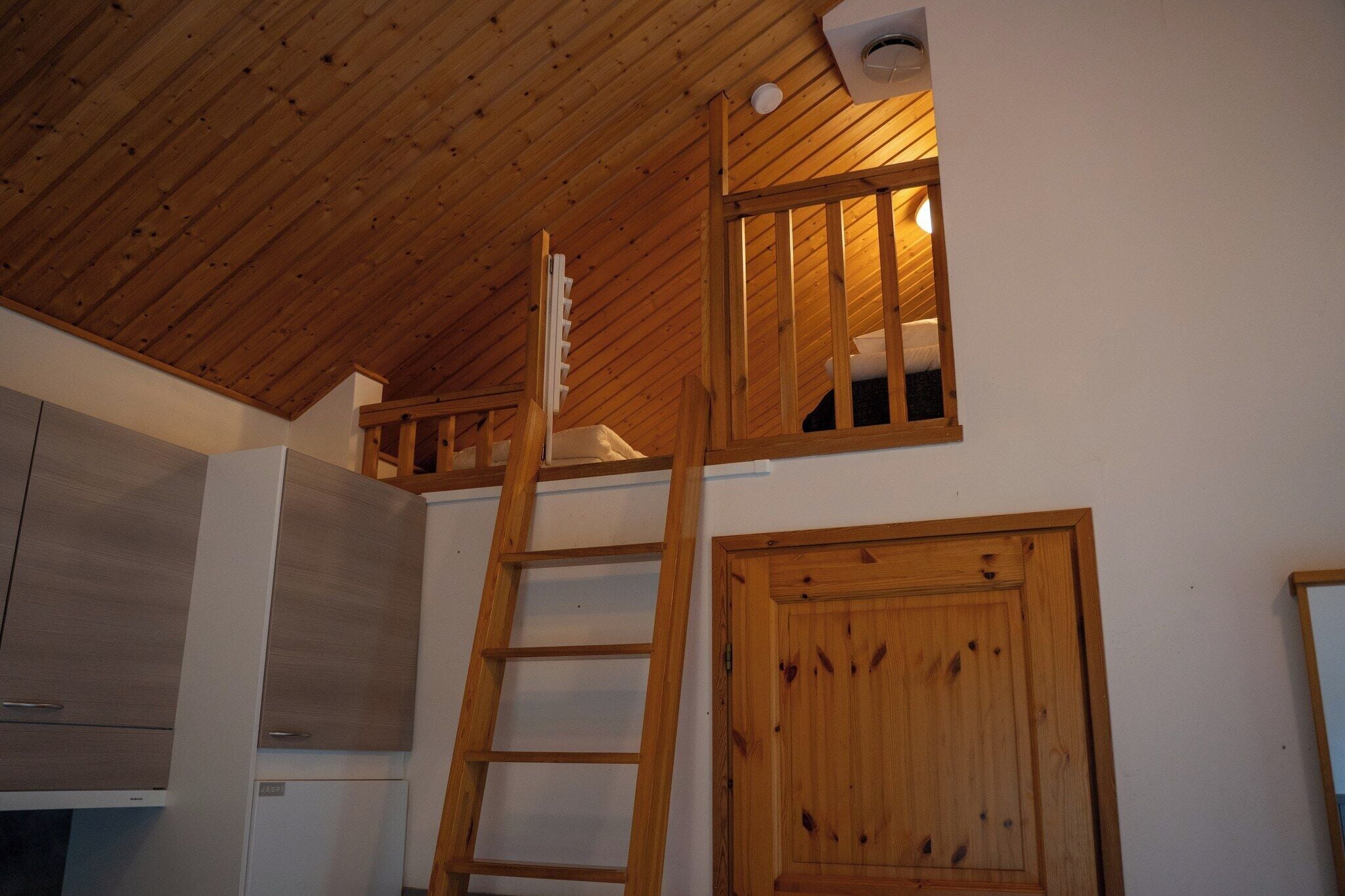 Quarto estilo loft com teto de madeira, escada e janela.
