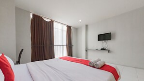 Quarto de hotel com cama bem arrumada, televisão na parede e janela com cortinas.