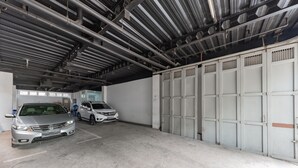 Uma garagem com dois carros estacionados em primeiro plano e uma grande porta de garagem ao fundo.