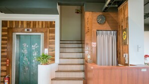 Um hall de hotel com um balcão de recepção em madeira, uma escada e uma porta de elevador verde com decorações florais.