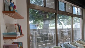 Um quarto com uma janela grande, cadeiras de vime, uma estante e uma mesa pequena.