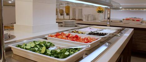 Buffet com diversas opções de comida, incluindo pepino fatiado, tomates e azeitonas.