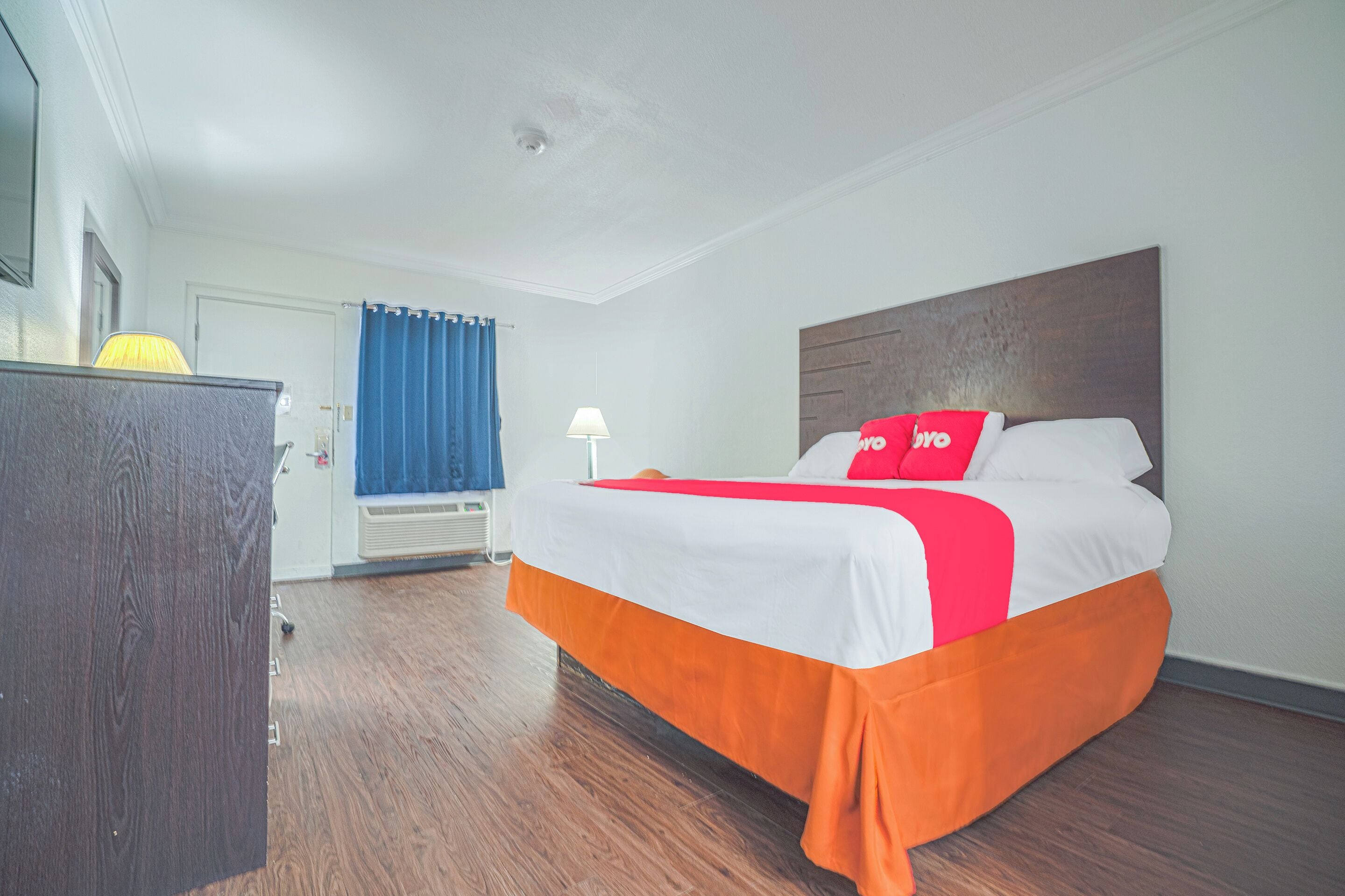 Quarto de hotel com cama, escrivaninha e janela com cortinas azuis.