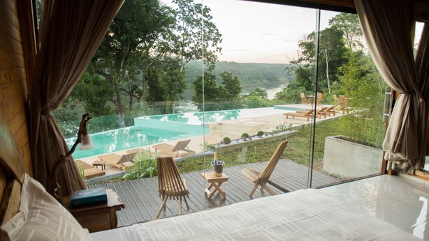 Quarto com cama grande, vista para uma piscina e área de estar ao ar livre.