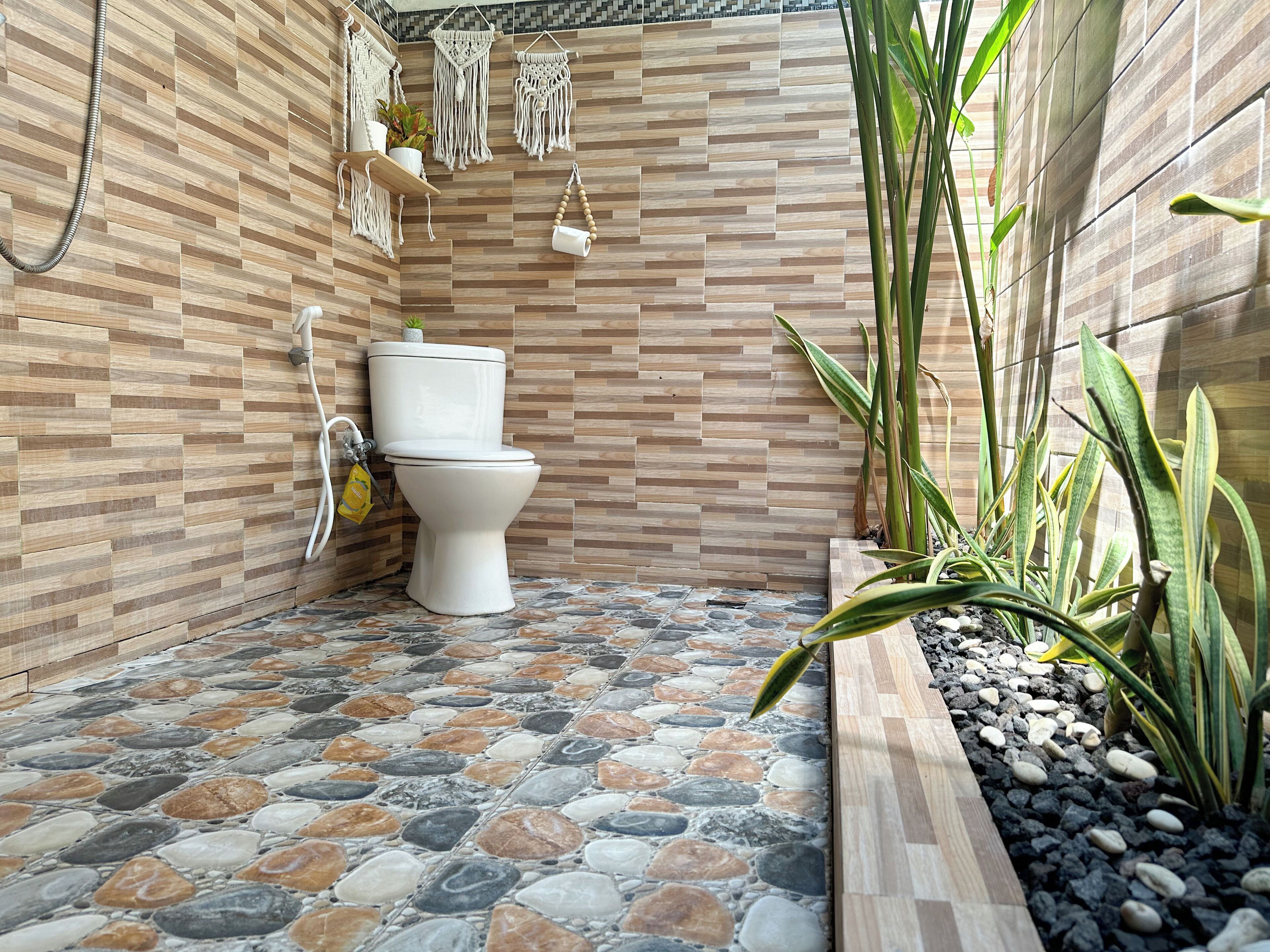 Casa de banho compacta com sanita, azulejos de madeira, soalho com padrão de pedra e um vaso de plantas.