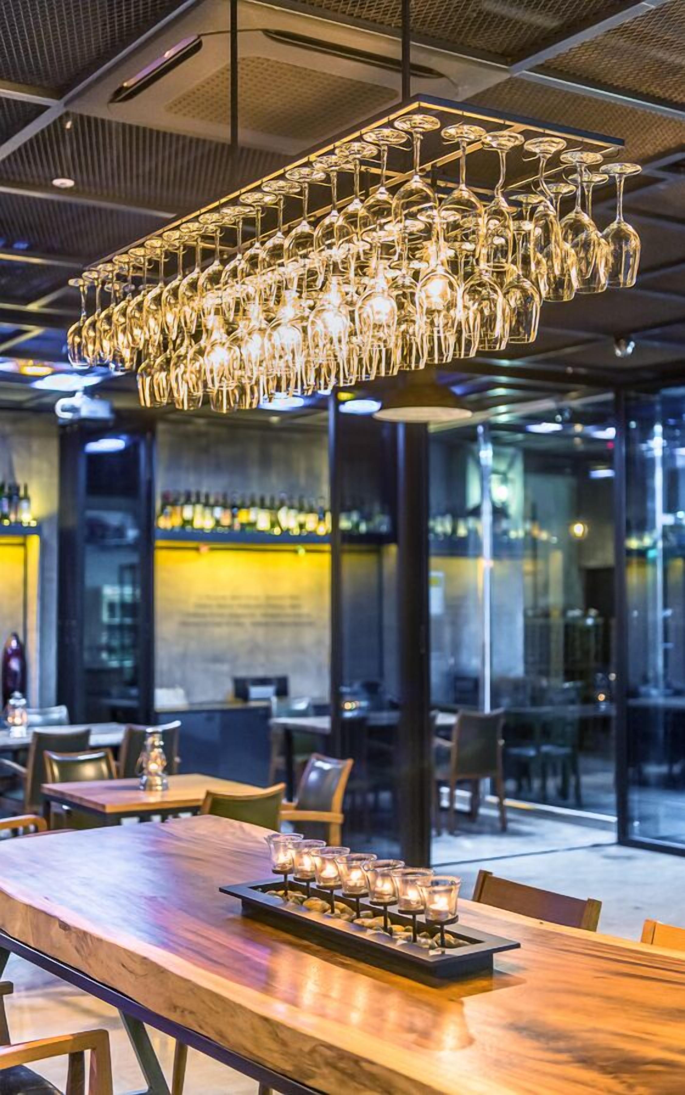 Interior moderno de restaurante com uma longa mesa de madeira, centros de mesa com velas e um lustre pendente único.