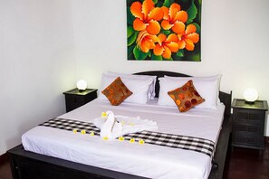Cama bem arrumada com lençóis brancos, dois travesseiros com estampas florais laranja e um arranjo de toalha em formato de cisne.