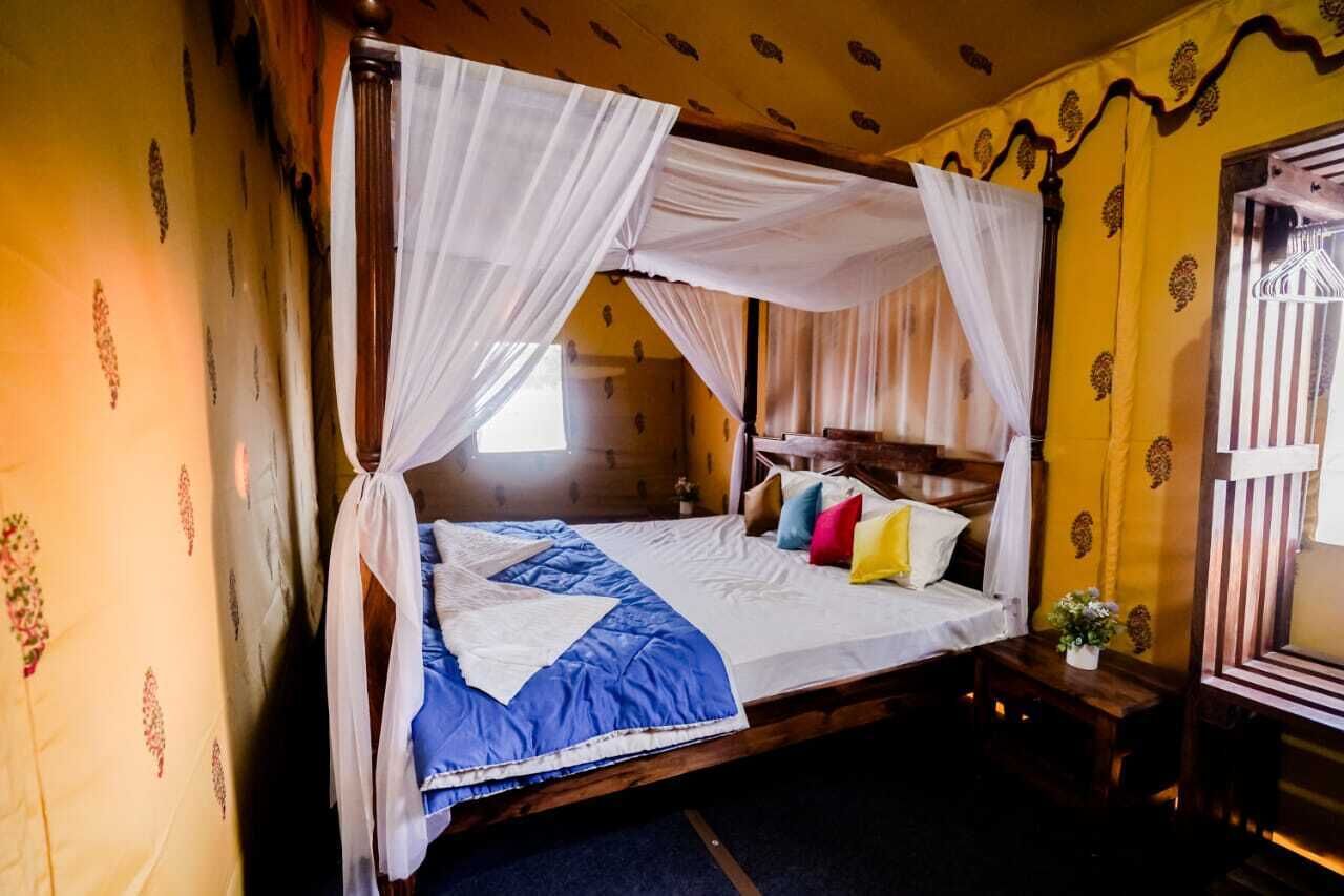 Uma cama de dossel com colchas brancas e azuis, uma cabeceira de madeira e uma pequena mesa de cabeceira com uma planta.