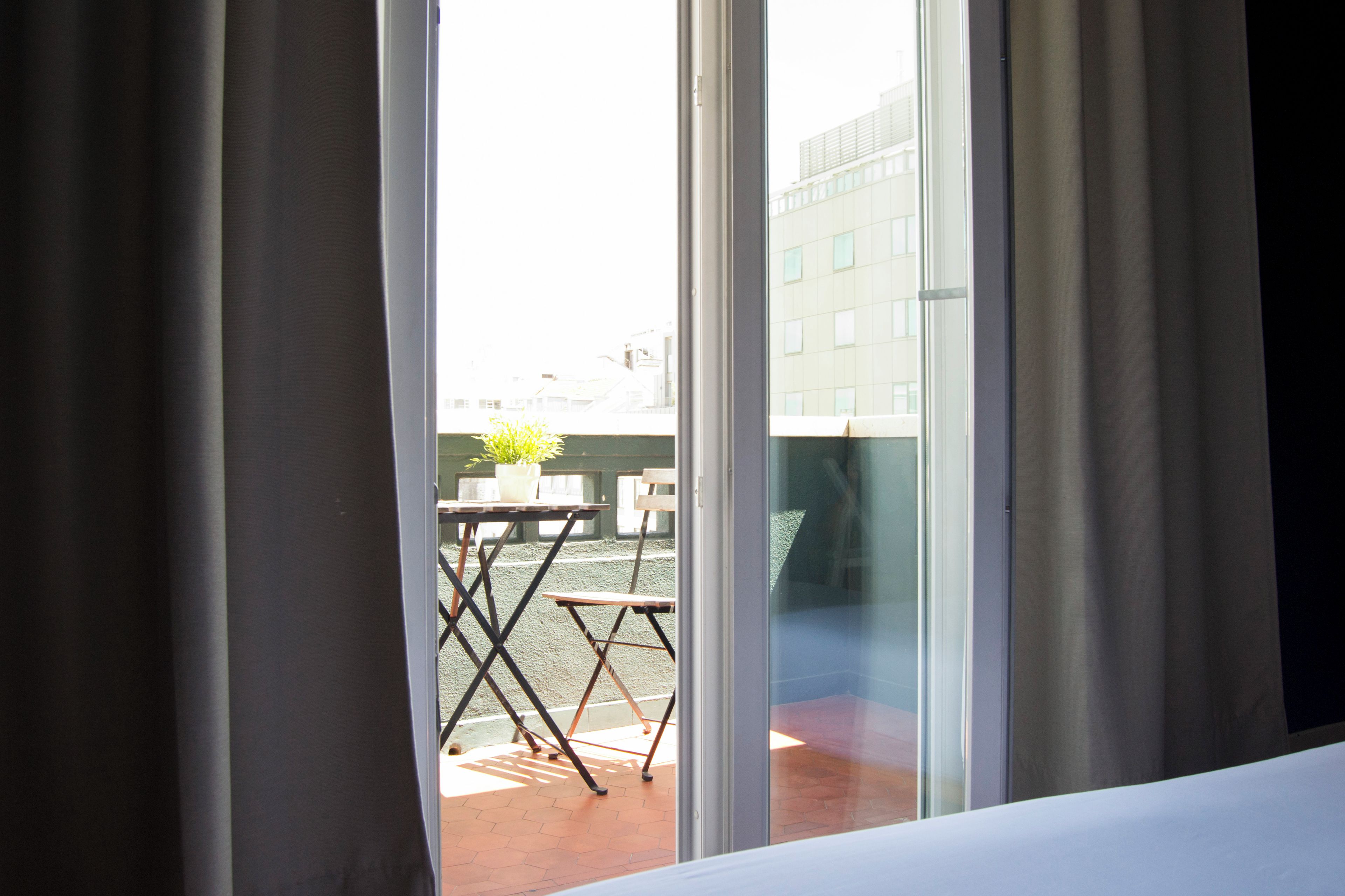Quarto de hotel com porta de vidro deslizante que dá para uma área externa com mesa e cadeiras.