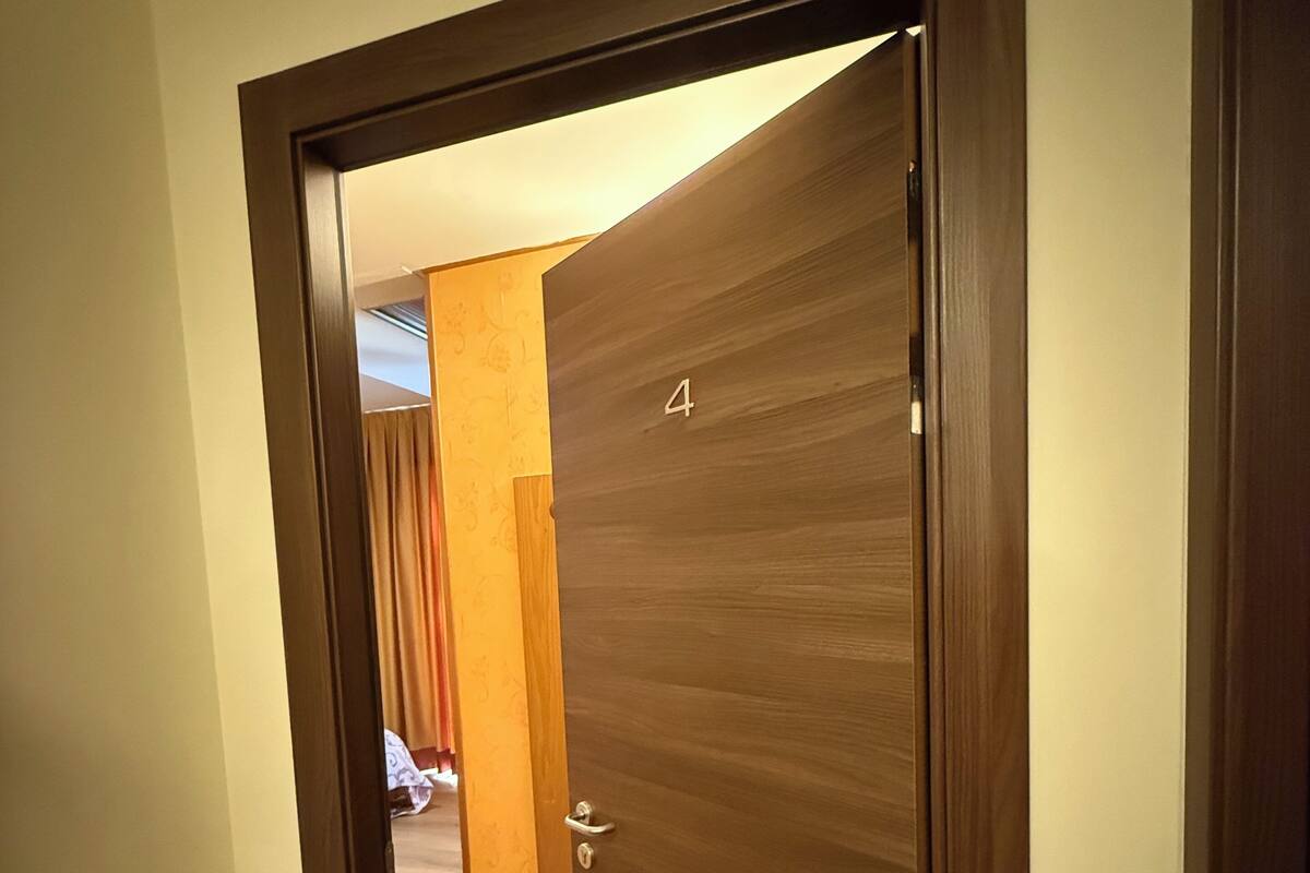 Uma porta de madeira com o número '4', dando acesso a um quarto com piso coberto por carpete.