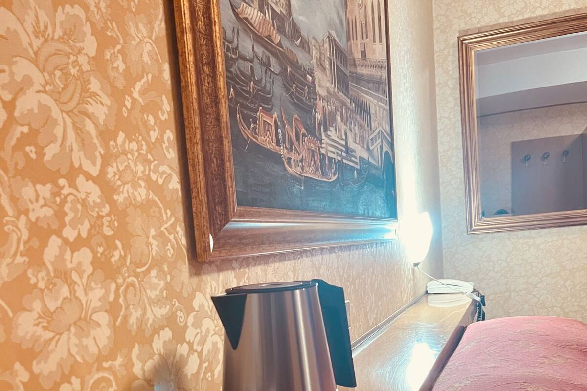 Quarto de hotel com uma cama, uma cafeteira, duas canecas e um tabuleiro com saquinhos de chá.