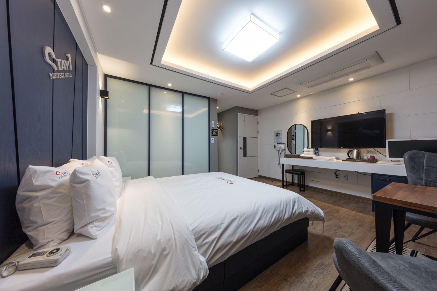 Quarto de hotel moderno com cama, escrivaninha, televisão e espelho.
