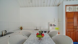 Cozinha moderna com armários brancos, bancada de mármore e área de jantar com mesa de mármore e cadeiras de vime.