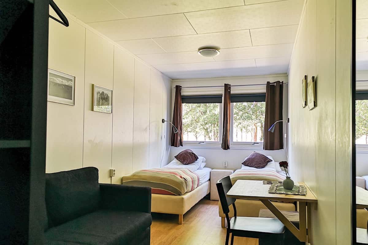 Quarto compacto com duas camas, um sofá, uma mesa e uma cadeira.