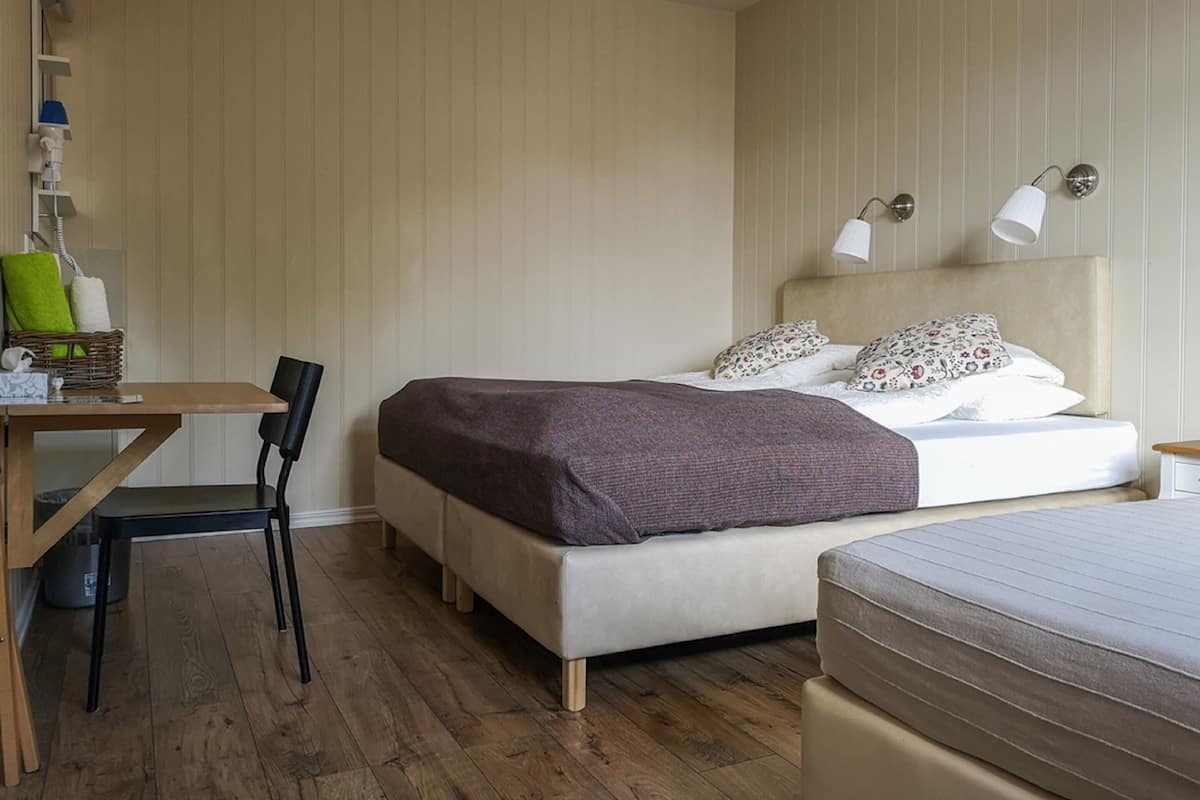 Quarto de hotel com cama, mesa de cabeceira, cadeira e pequena escrivaninha com luminária.