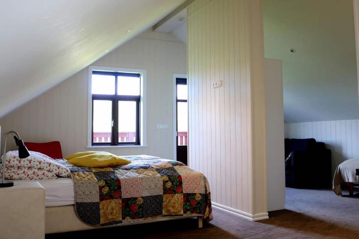 Quarto com cama, mesa de cabeceira, abajur, janela e porta.