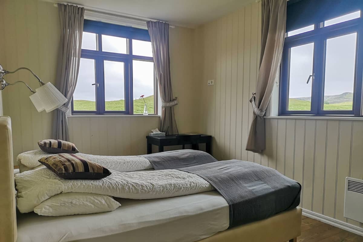 Quarto com duas camas, mesa de cabeceira, abajur e vista para o exterior.