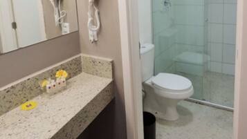 Casa de banho com chuveiro, sanita e toucador com espelho e secador de cabelo.