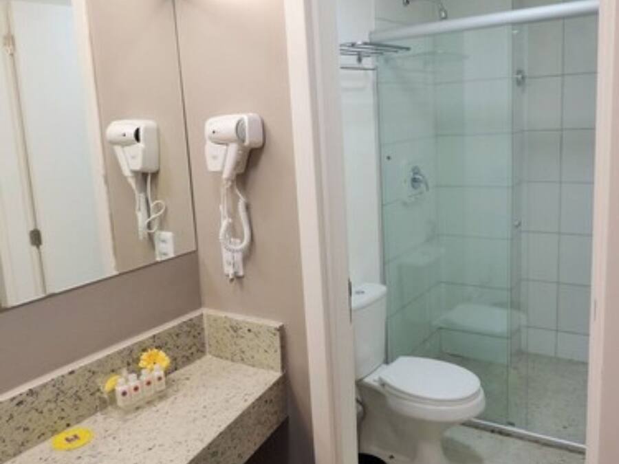 Casa de banho com chuveiro, sanita e toucador com espelho e secador de cabelo.