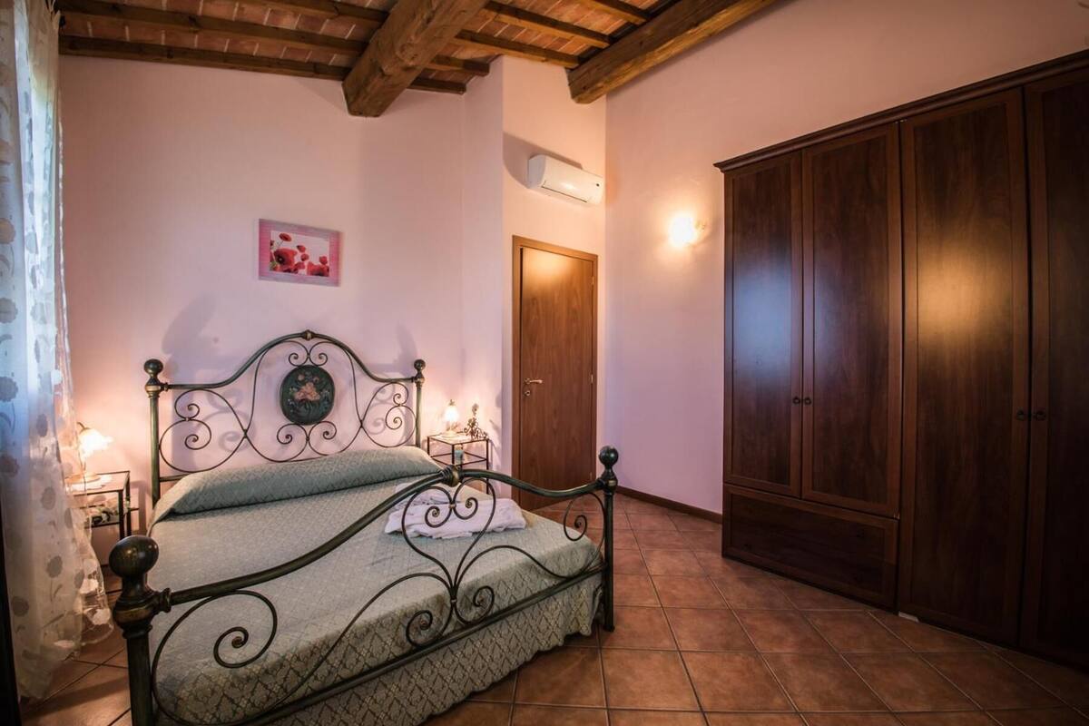 Quarto com cama de estrutura metálica, guarda-roupa de madeira e porta com um aparelho de ar condicionado em cima.