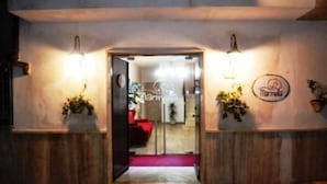 Entrada de hotel com porta de vidro, plantas em vasos de ambos os lados e um letreiro acima da porta.