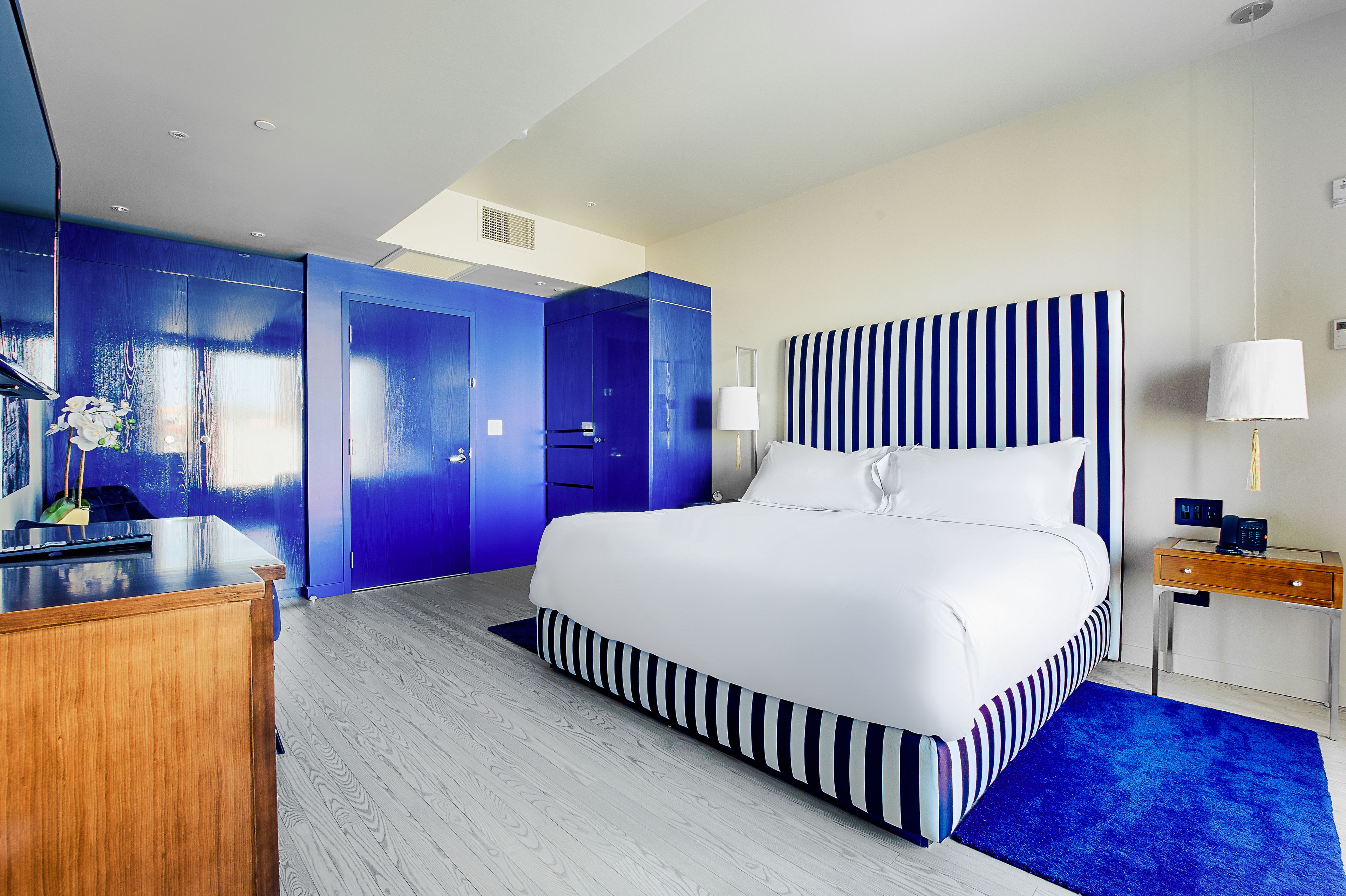 Quarto de hotel moderno com uma cama grande, uma escrivaninha de madeira e uma parede azul decorativa.