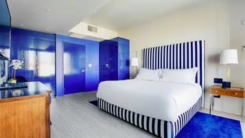 Quarto de hotel moderno com uma cama grande, uma escrivaninha de madeira e uma parede azul decorativa.