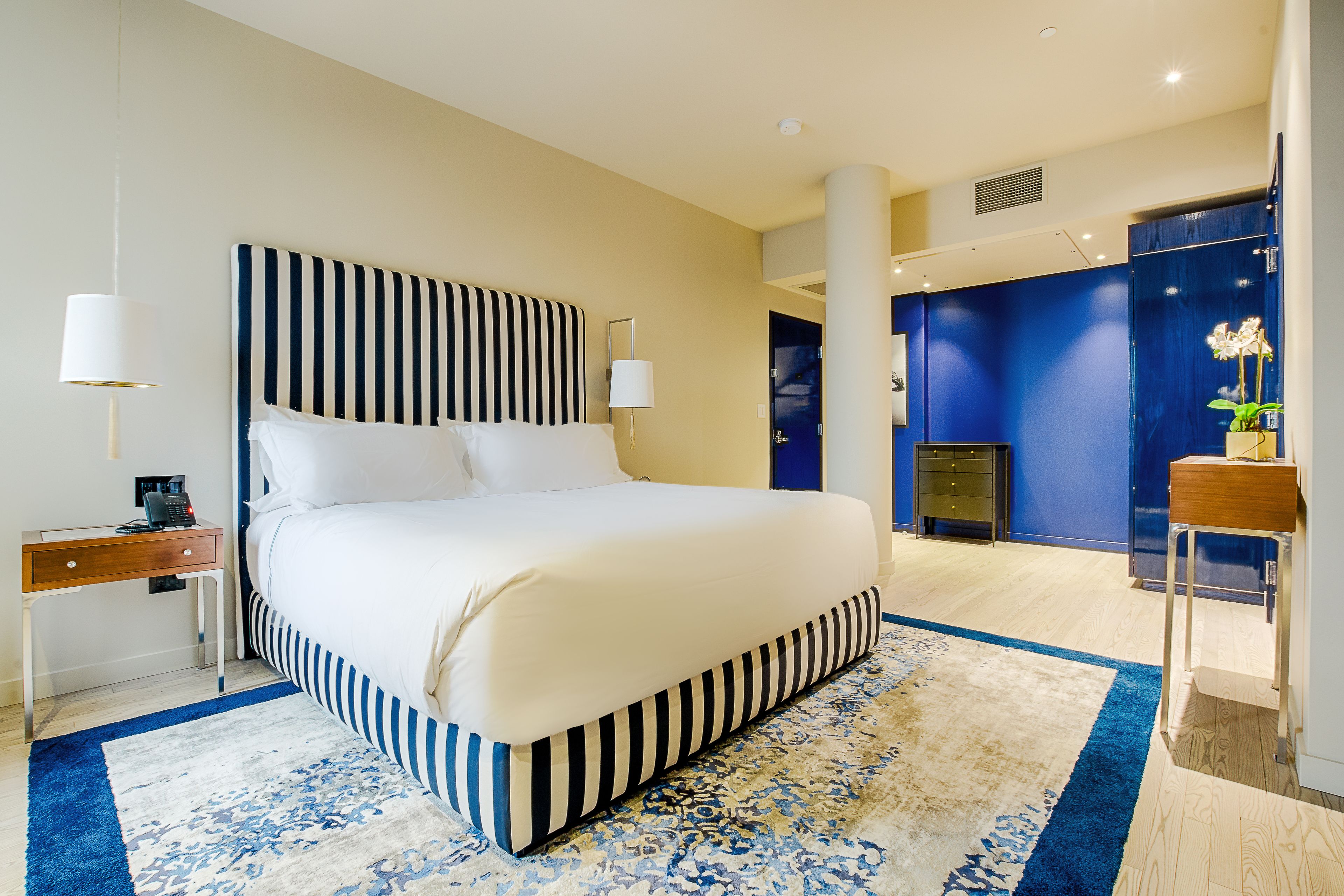 Quarto de hotel moderno com uma cama grande, uma mesa de escritório e uma mesinha de cabeceira.