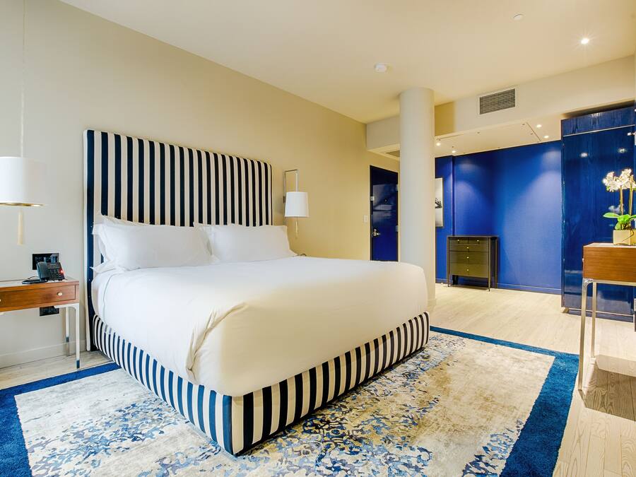 Quarto de hotel moderno com uma cama grande, uma mesa de escritório e uma mesinha de cabeceira.