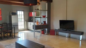 Uma sala de estar moderna com área de jantar, cozinha com armários vermelhos, televisão de tela plana e uma janela com luz natural.