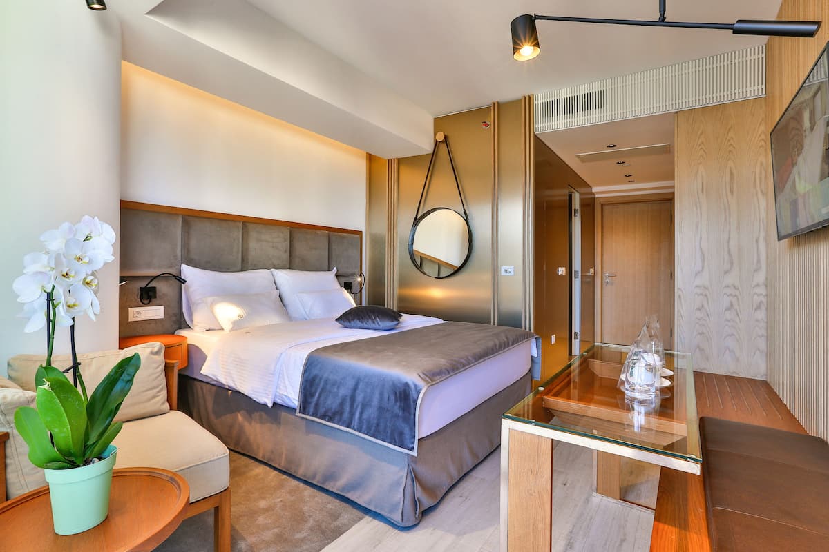 Quarto de hotel moderno com uma cama grande, mesa de cabeceira e um pequeno espaço de estar.