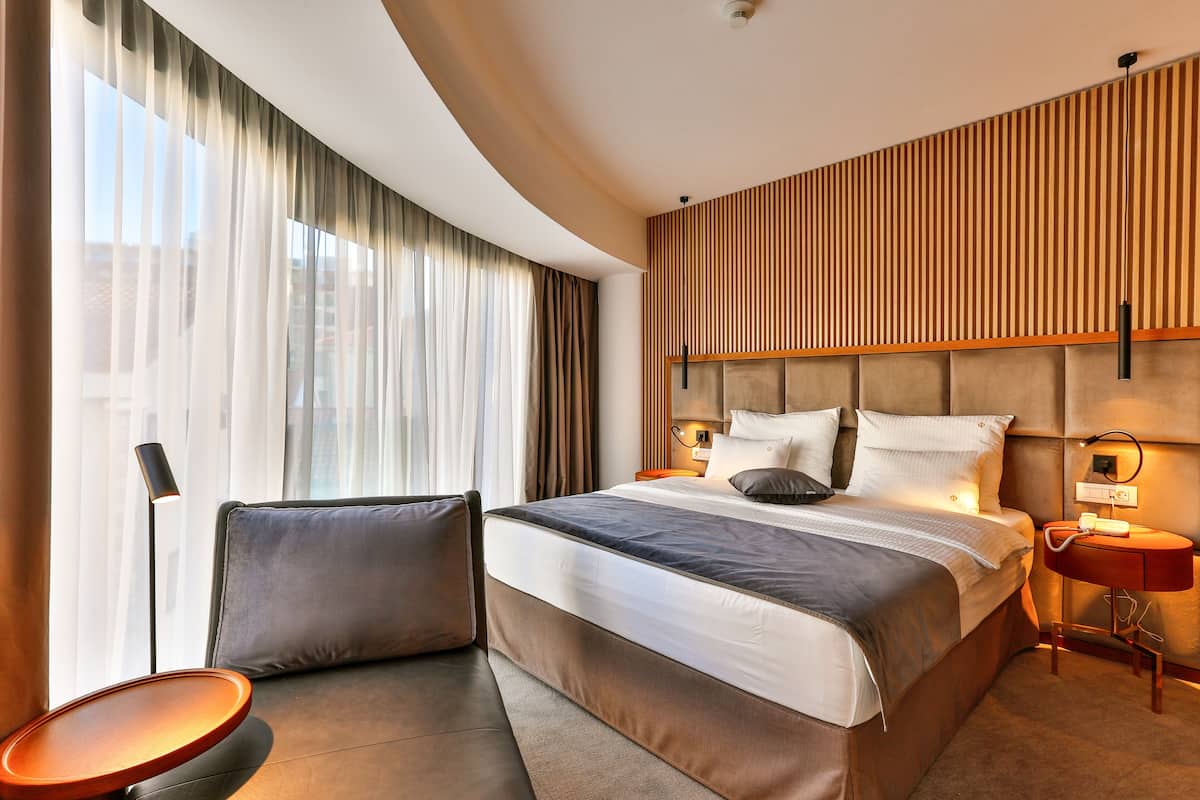Quarto de hotel moderno com uma cama grande, um sofá, uma mesa de cabeceira e um abajur.