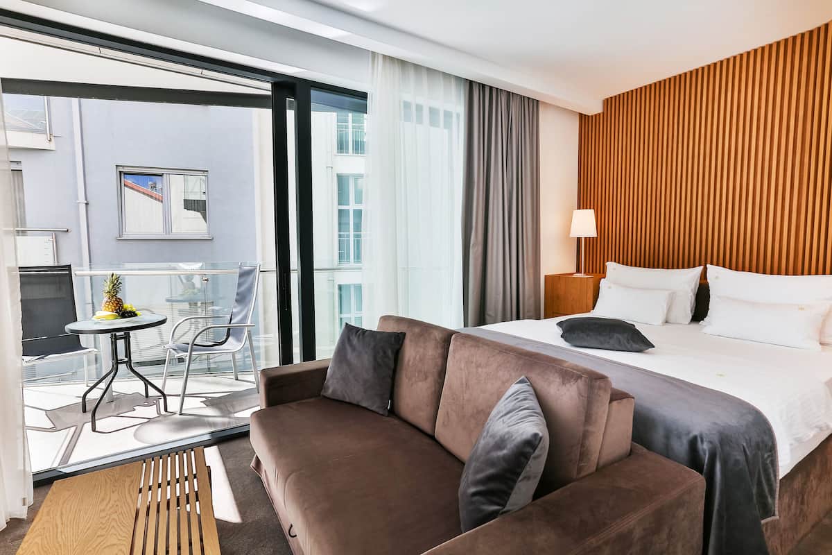 Quarto de hotel com cama grande, sofá, pequena mesa com uma abacaxi e varanda com porta de vidro.