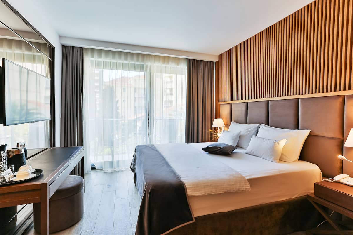 Quarto de hotel com uma cama grande, uma escrivaninha, uma televisão e uma janela com cortinas.