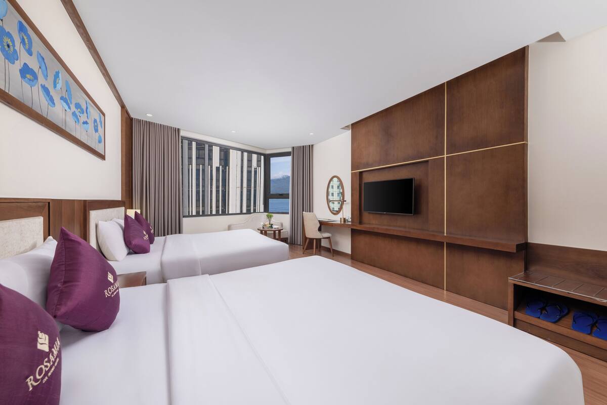 Quarto de hotel com duas camas, televisão, escrivaninha e janela com vista.