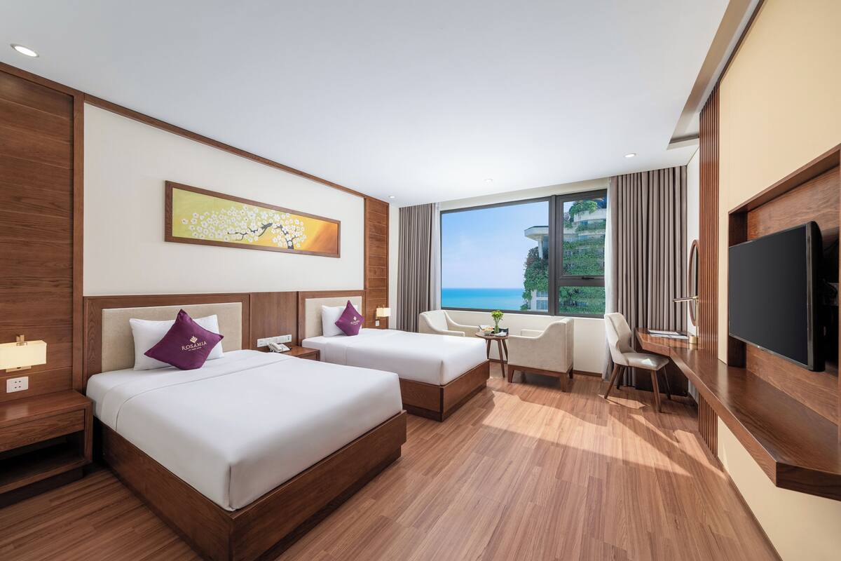 Quarto de hotel com duas camas, uma escrivaninha, televisão e uma janela grande com vista.