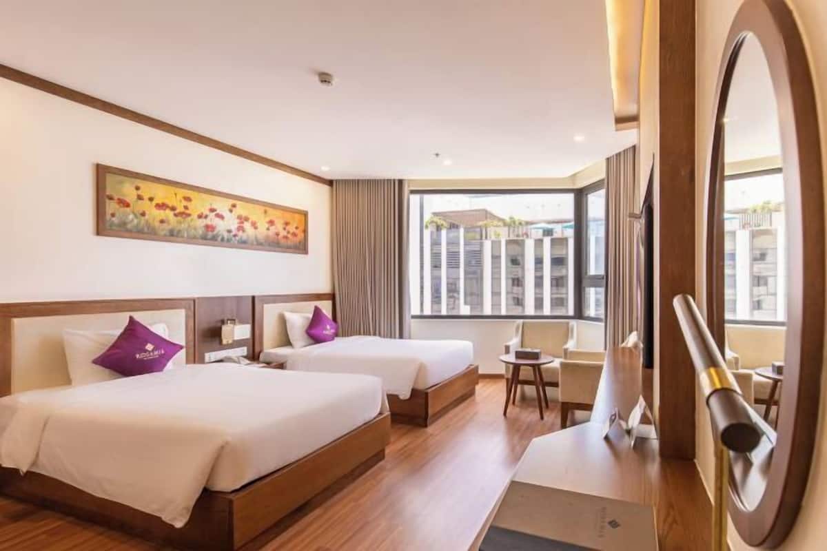 Quarto de hotel com duas camas, um quadro na parede, uma janela com vista e uma porta com espelho.