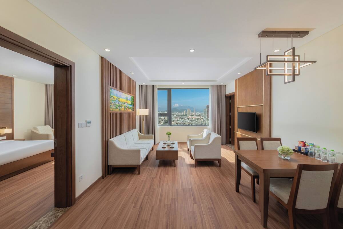 Quarto de hotel moderno com vista para a cidade, um sofá, uma mesa de jantar e uma televisão.