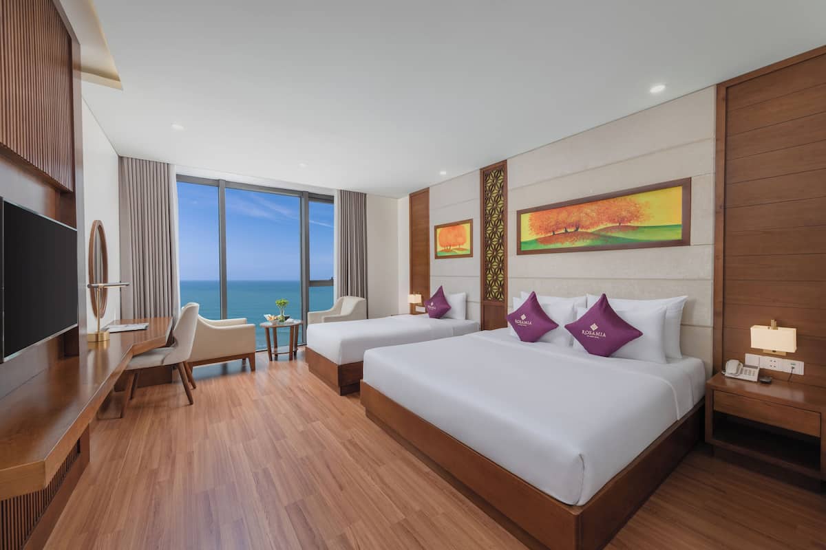 Quarto de hotel com duas camas, televisão, secretária e vista para o mar.